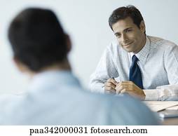 Two people sitting across from each other at table, looking at document ...